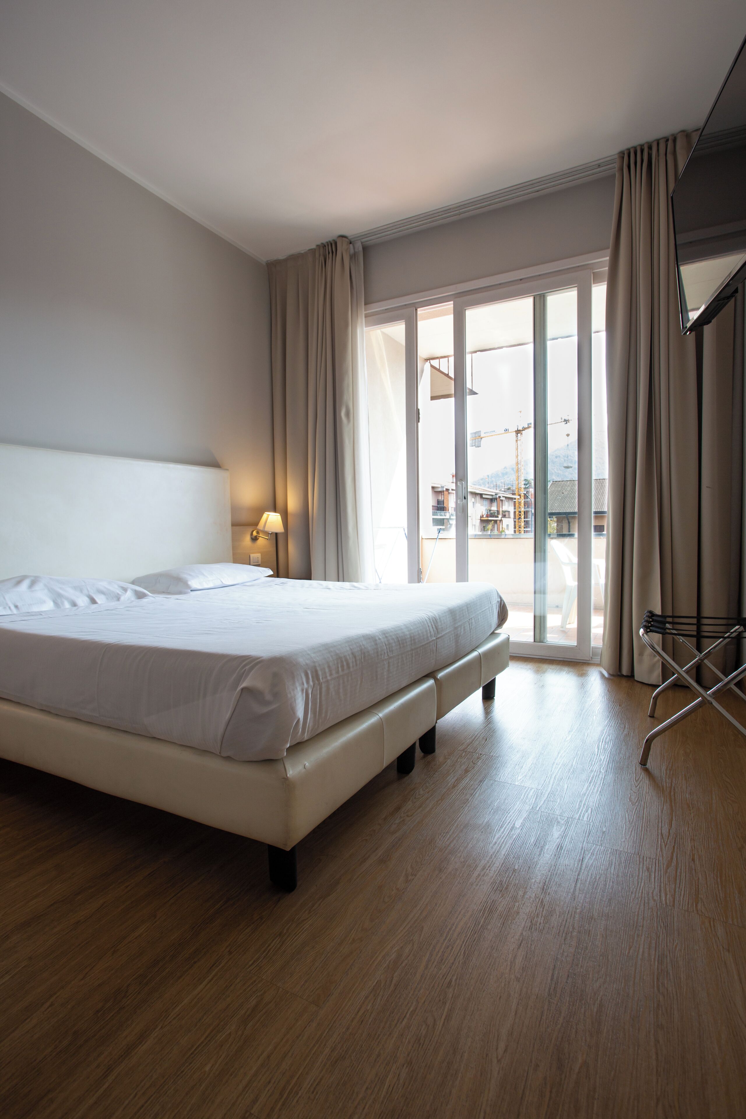 Quarto de hotel com uma cama grande, uma mesa de cabeceira com abajur, uma porta de vidro deslizante para o exterior e uma cadeira de metal.