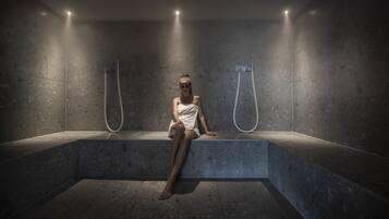 Uma pessoa sentada numa área de chuveiro moderna e pouco iluminada, com um banco e duas cabeças de chuveiro.