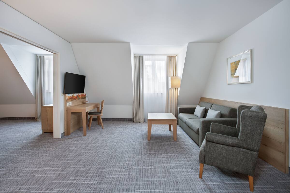 Quarto de hotel com escrivaninha, televisão, sofá e luminária.