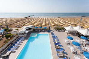 Uma área de piscina com espreguiçadeiras e guarda-sóis, uma praia com guarda-sóis e um píer ao fundo.