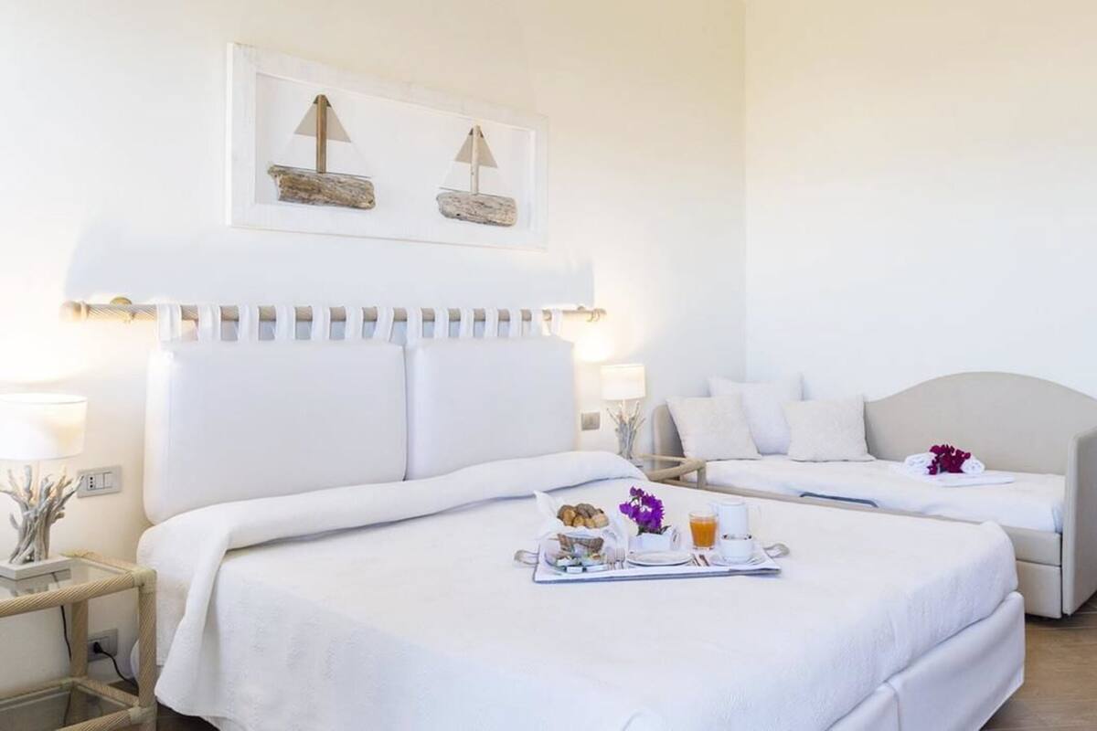 Quarto de hotel com duas camas, uma pequena mesa com itens de café da manhã e um objeto decorativo acima das camas.