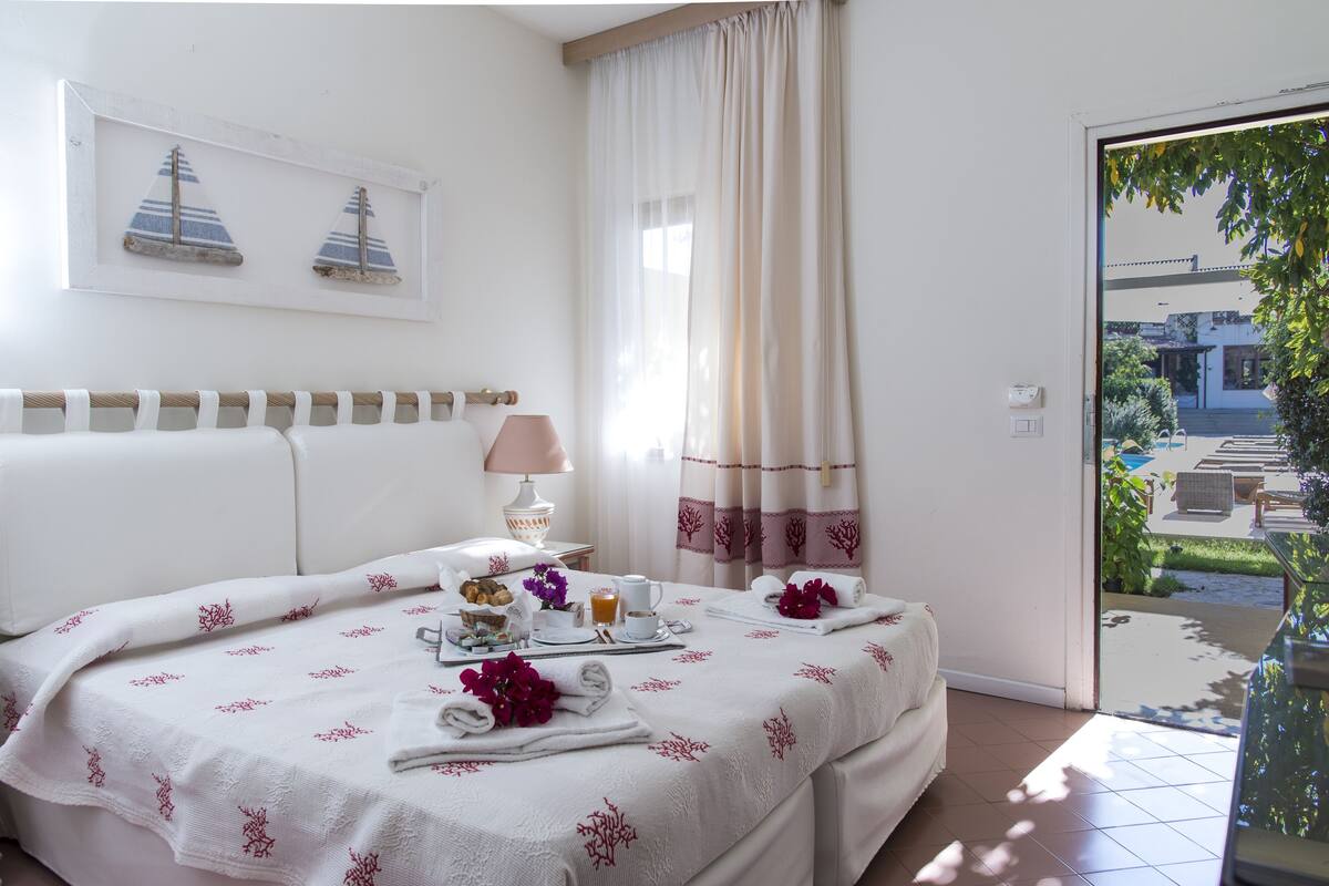 Quarto de hotel com uma cama, uma mesa com itens de café da manhã, uma luminária e vista para o exterior.
