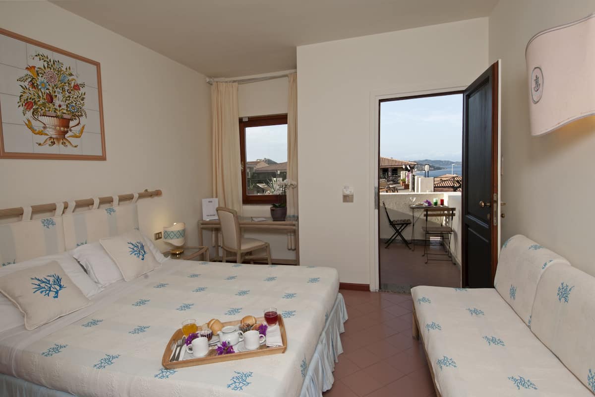 Quarto de hotel com uma cama grande, um sofá menor, área de jantar e vista para o mar.