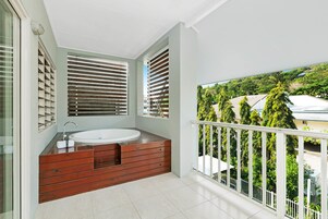 Uma varanda com vista para uma área residencial, uma banheira de madeira e uma janela com persianas.