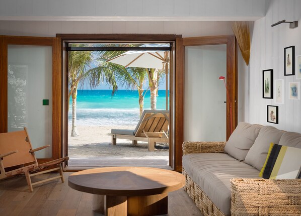 Quarto com vista para a praia, uma cadeira de madeira, um sofá e uma mesa redonda.