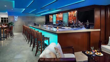 Uma área de bar moderna com balcão extenso, banquetas e um espaço de estar com sofá e cadeiras.