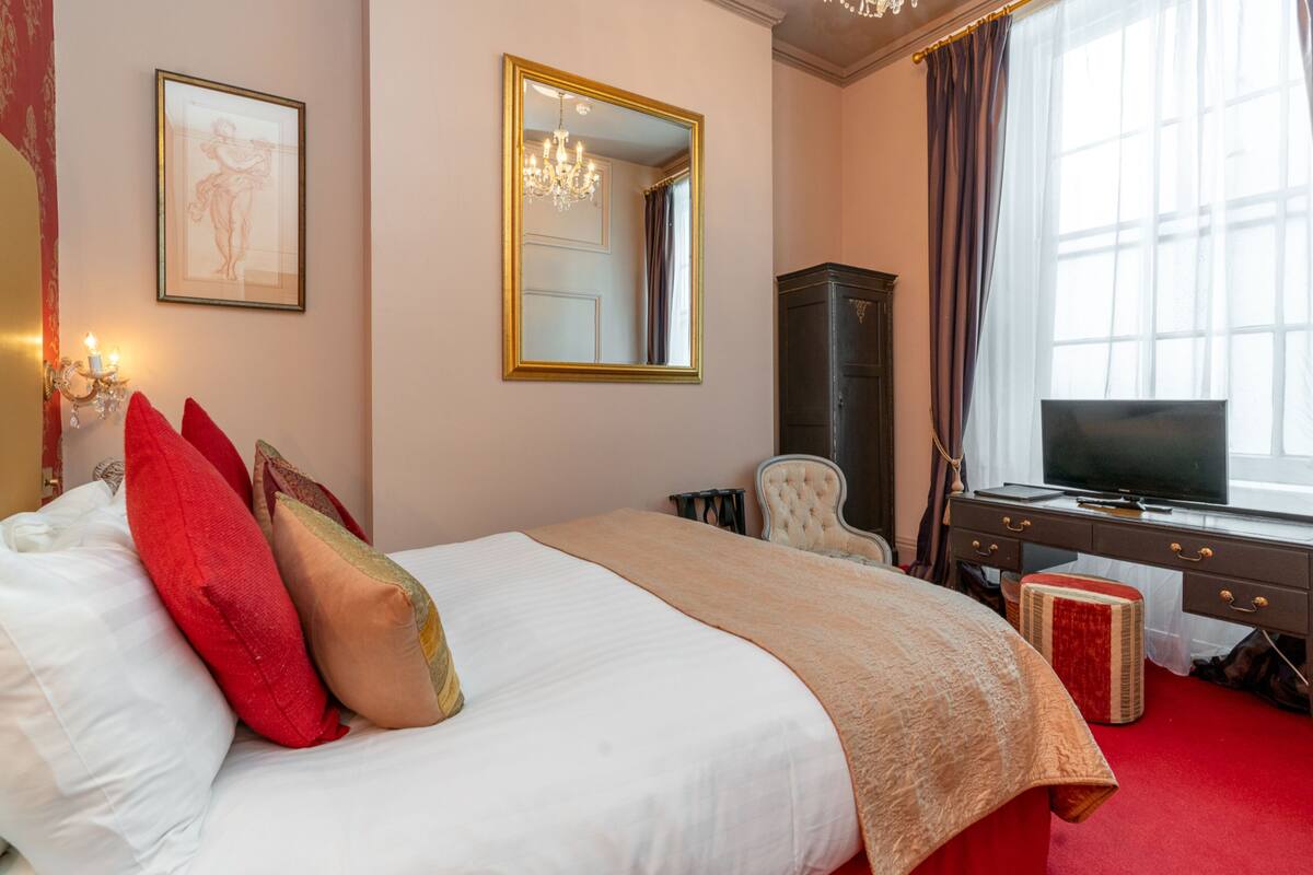 Quarto de hotel com uma cama grande, televisão, escrivaninha e uma cadeira.