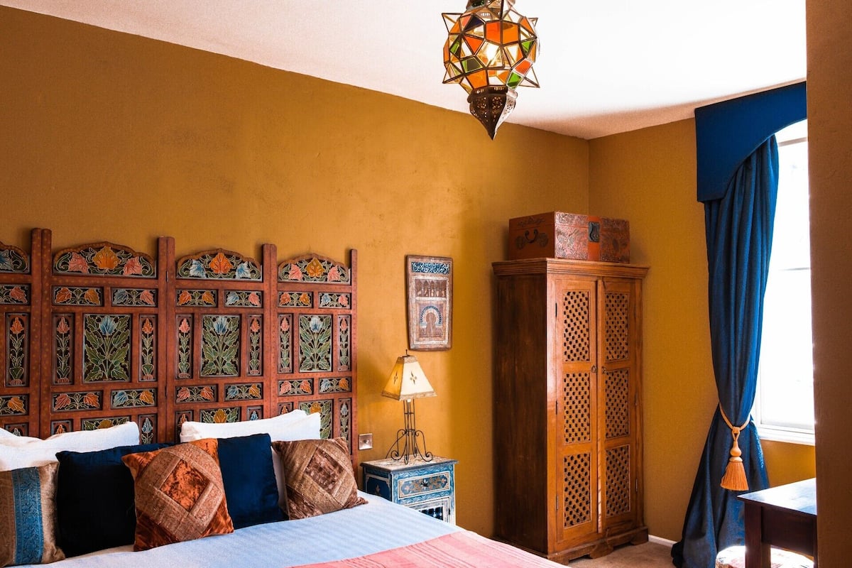 Quarto com cama, armário de madeira, parede com entalhes detalhados e luminária suspensa.