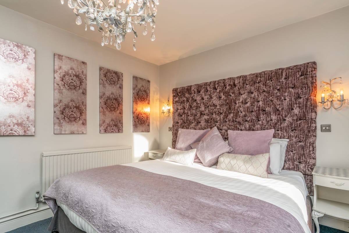 Quarto com cama grande, um candelabro, arandelas na parede e obra de arte com padrão floral.