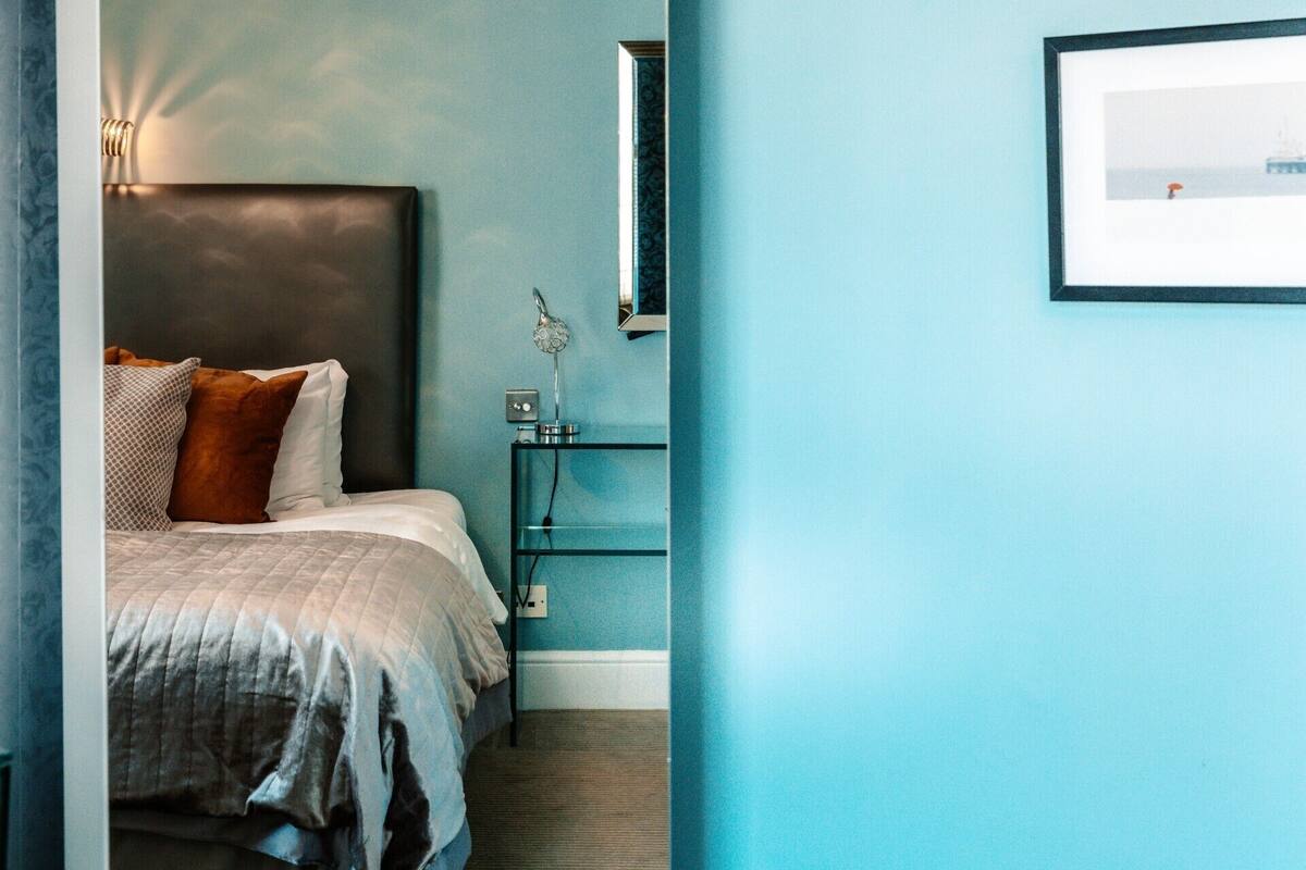 Quarto com cama, mesa de cabeceira, espelho fixado na parede e quadro emoldurado.