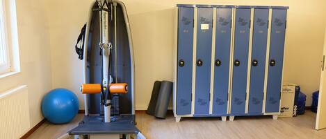 Uma academia com equipamentos de ginástica, uma bola de exercício azul e uma fileira de armários.