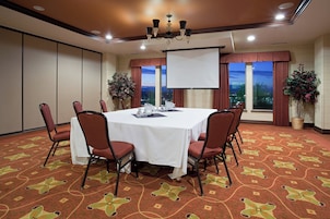 Uma sala de conferências com uma mesa branca, cadeiras vermelhas, uma tela de projetor e vista para a cidade ao entardecer.