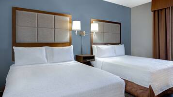 Quarto de hotel com duas camas, cada uma com cabeceira e mesa de cabeceira com abajur.