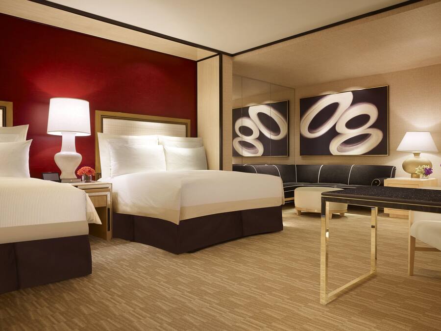 Quarto de hotel com duas camas, uma escrivaninha, um sofá e um espelho grande.