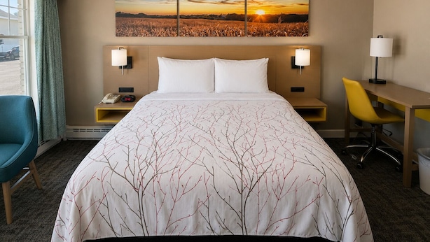 Quarto de hotel com uma cama grande, duas luminárias de cabeceira, uma escrivaninha com cadeira e vista para uma paisagem com pôr do sol.
