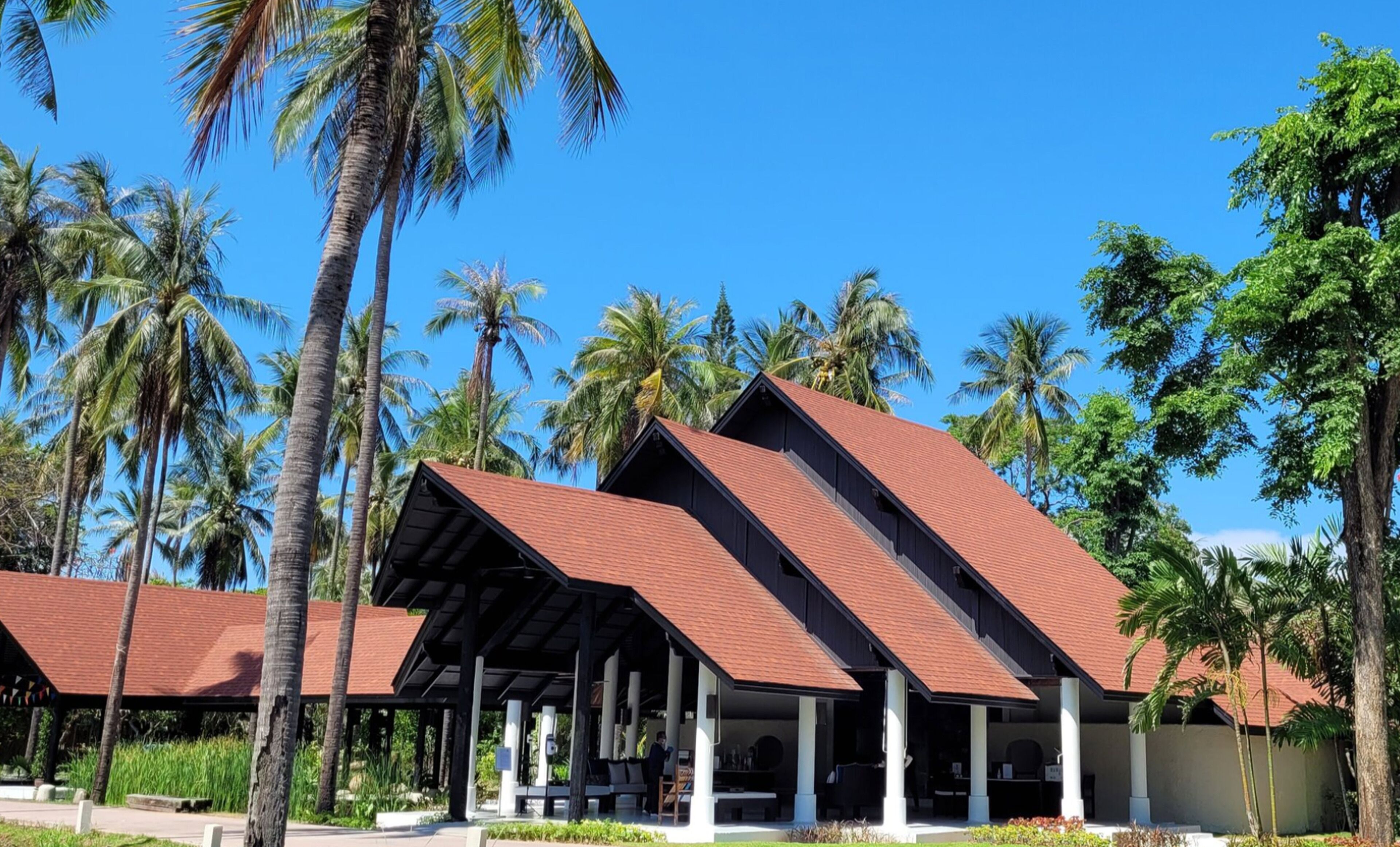 Resort com vários edifícios com telhados vermelhos e colunas brancas, cercado por palmeiras e vegetação.