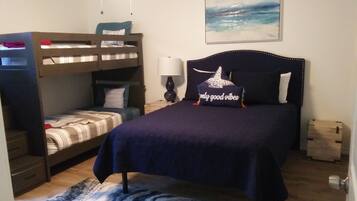 Quarto com beliches, uma cama com almofada 'only good vibes', uma luminária e um quadro na parede.