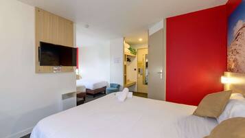 Quarto de hotel com cama, televisão presa na parede, escrivaninha com cadeira e parede em destaque vermelha.