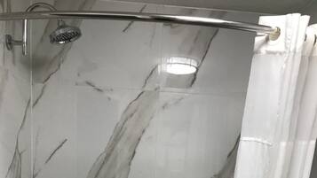 Um banheiro com chuveiro em box de vidro, paredes de mármore e banheira branca.