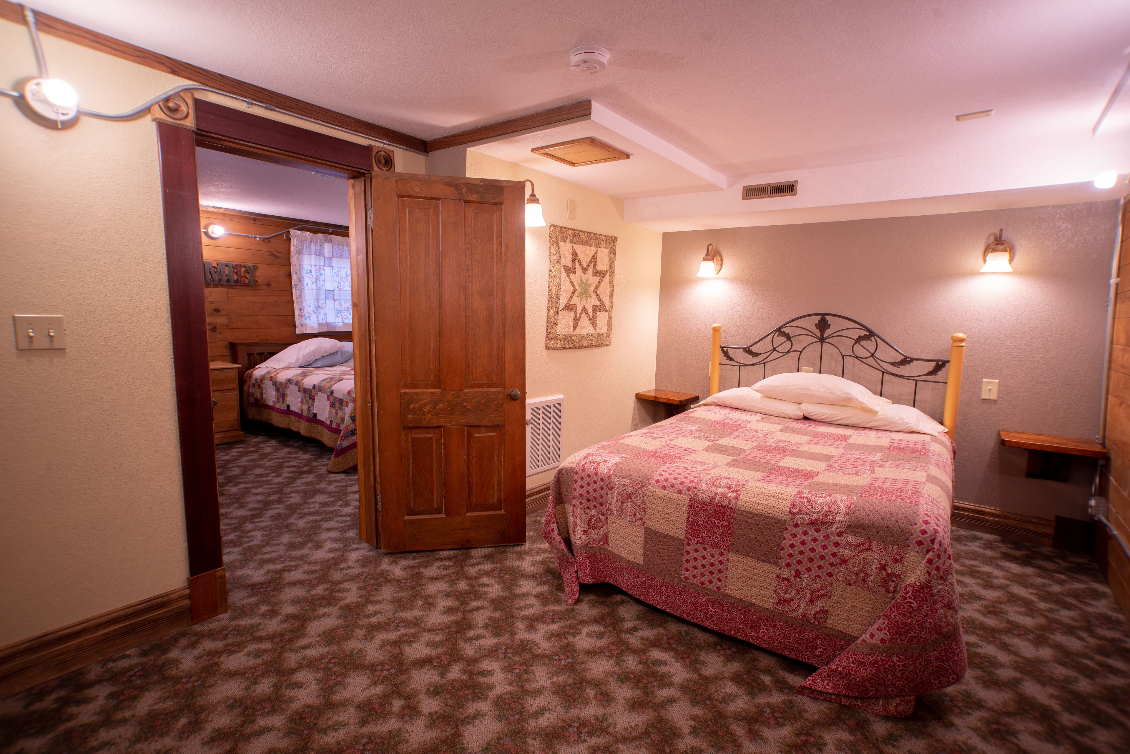 Quarto com cama, porta de madeira, radiador e luminária fixada na parede.
