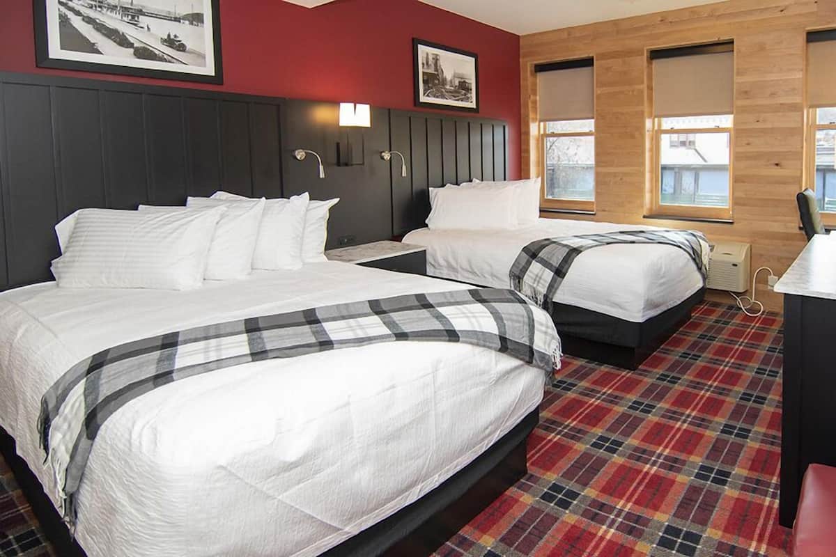 Quarto de hotel com duas camas, uma parede de destaque vermelha e um tapete xadrez.