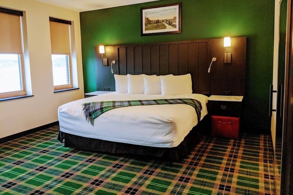 Quarto de hotel com cama grande, paredes verdes, um quadro emoldurado e uma janela.