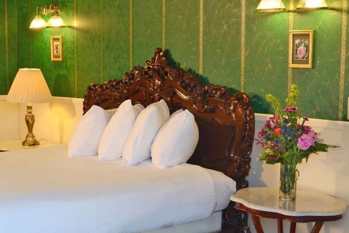 Uma cama com cabeceira de madeira, roupa de cama branca, um abajur e um vaso com flores.