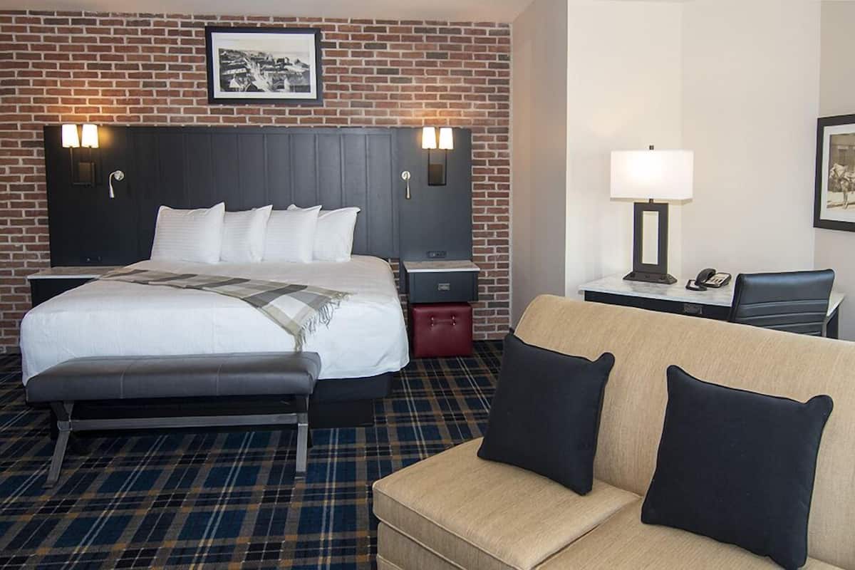 Quarto de hotel com uma cama grande, um sofá, uma mesa de cabeceira, um abajur e uma parede de tijolos.