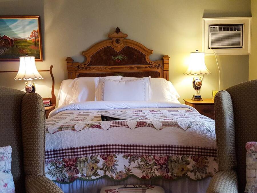 Uma cama bem arrumada com um edredom floral, duas luminárias de cabeceira, um quadro na parede e um ar condicionado.
