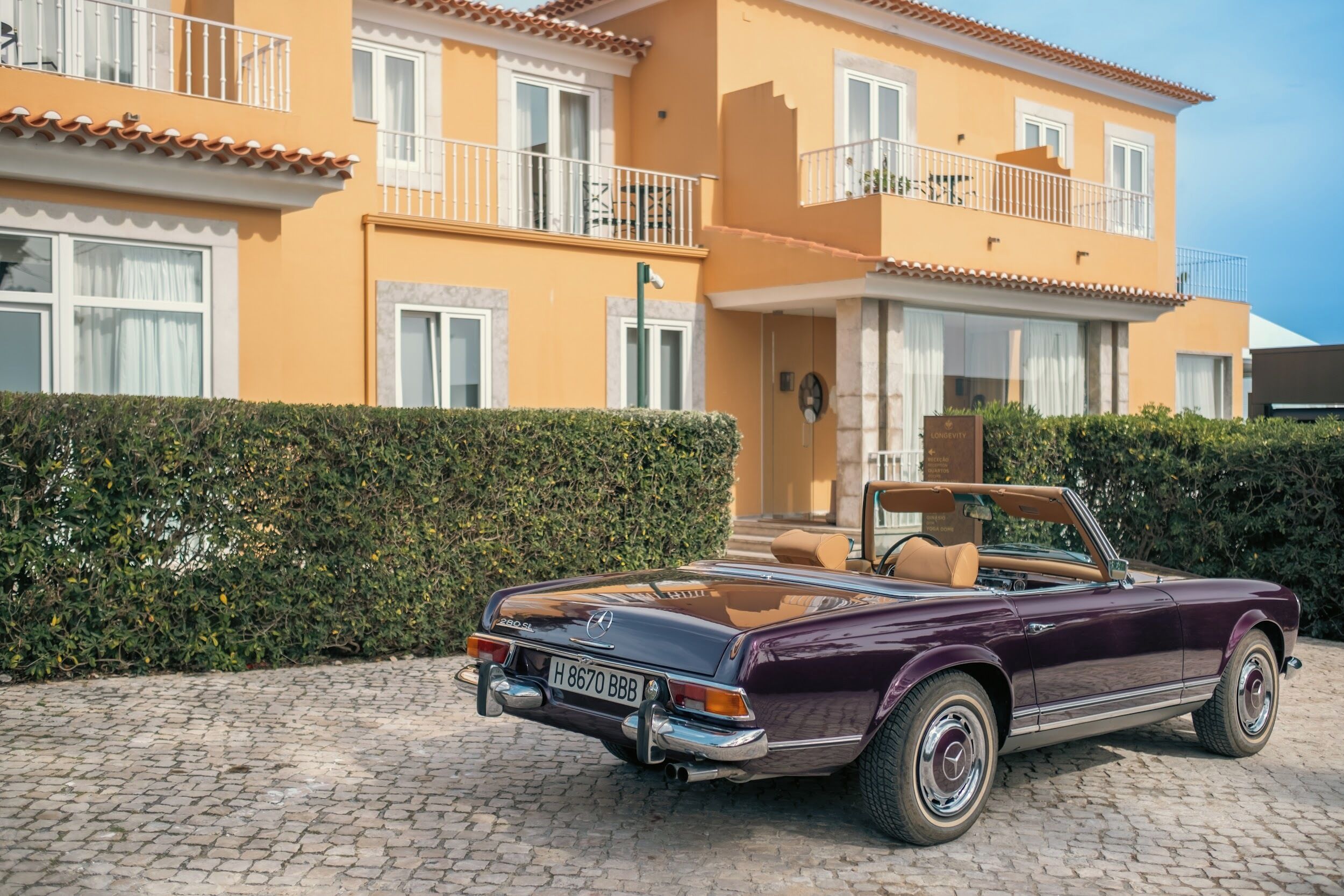 Um carro conversível clássico roxo estacionado em frente a um edifício amarelo com varandas.