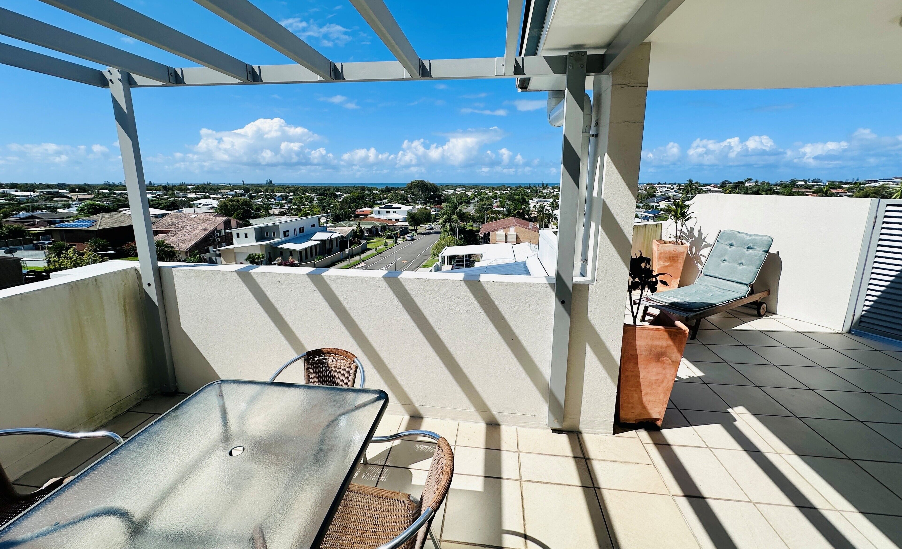 Varanda com vista para uma área residencial, uma cadeira, uma mesa e um vaso com planta.