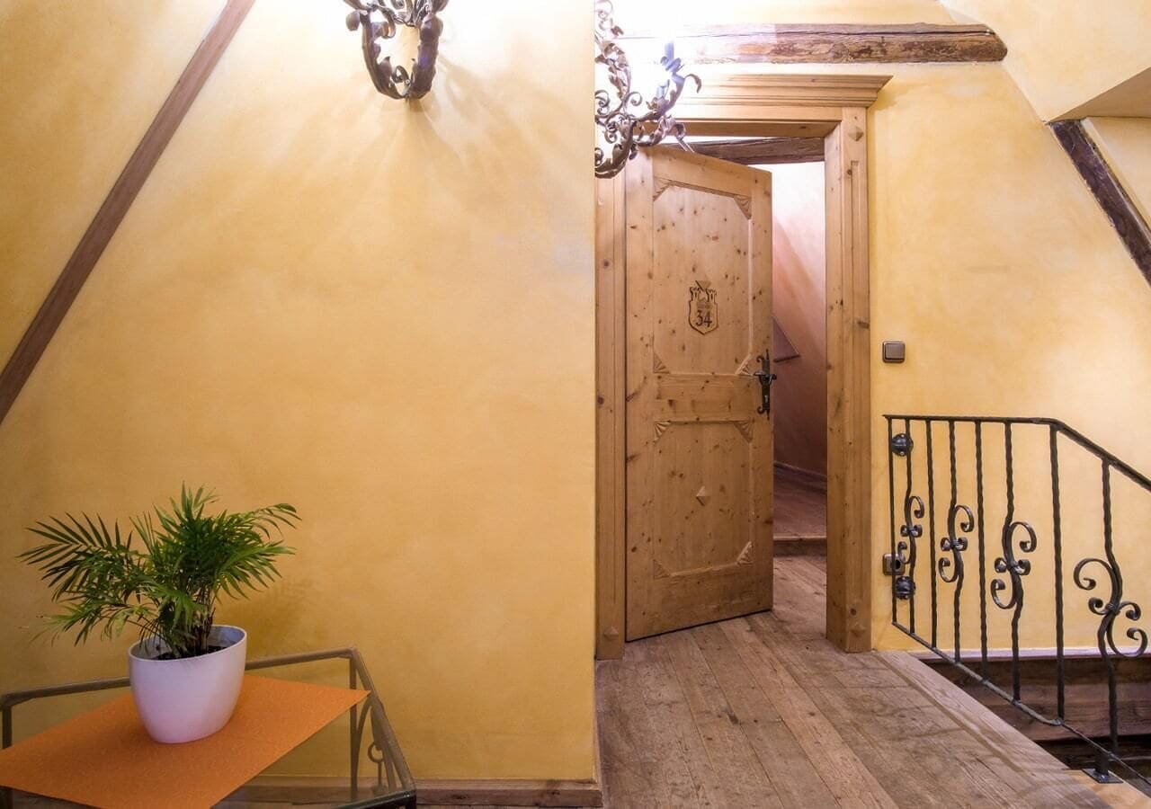 Uma porta de madeira com um número, uma escadaria com grades de ferro forjado e um vaso de planta sobre uma mesa.