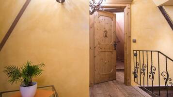 Uma porta de madeira com um número, uma escadaria com grades de ferro forjado e um vaso de planta sobre uma mesa.