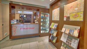 Uma área de recepção com balcão identificado como 'rosarosae', uma vitrine de vidro e folhetos informativos.