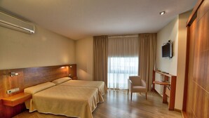 Quarto de hotel com duas camas, uma mesa, uma cadeira, uma televisão e janela com cortinas.