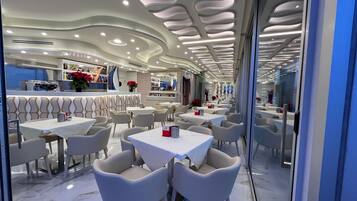 Restaurante moderno com mesas redondas e cadeiras acolchoadas, área de bar e teto decorativo.