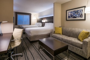 Quarto de hotel com duas camas, um sofá, uma mesa de centro, uma escrivaninha e uma cadeira.