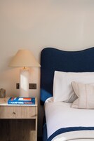 Quarto de hotel bem arrumado com uma cama, mesa de cabeceira com abajur e um livro intitulado 'HAMPTON'S PRIVATE'.