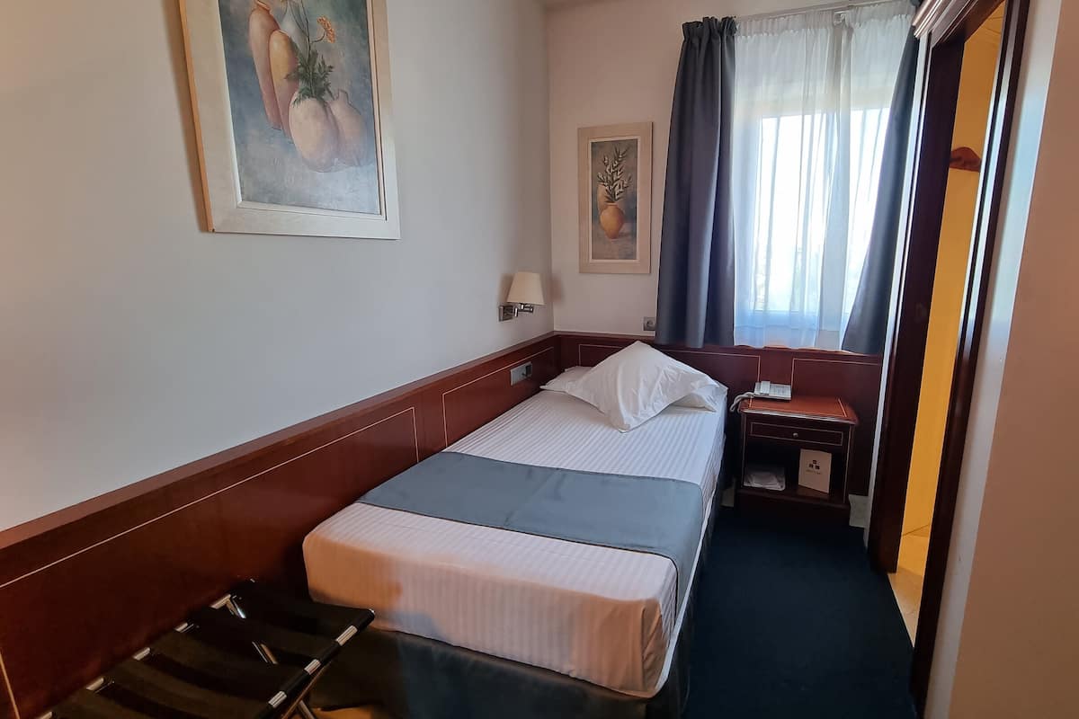 Quarto de hotel com uma cama, uma mesinha de cabeceira, um abajur e um quadro na parede.