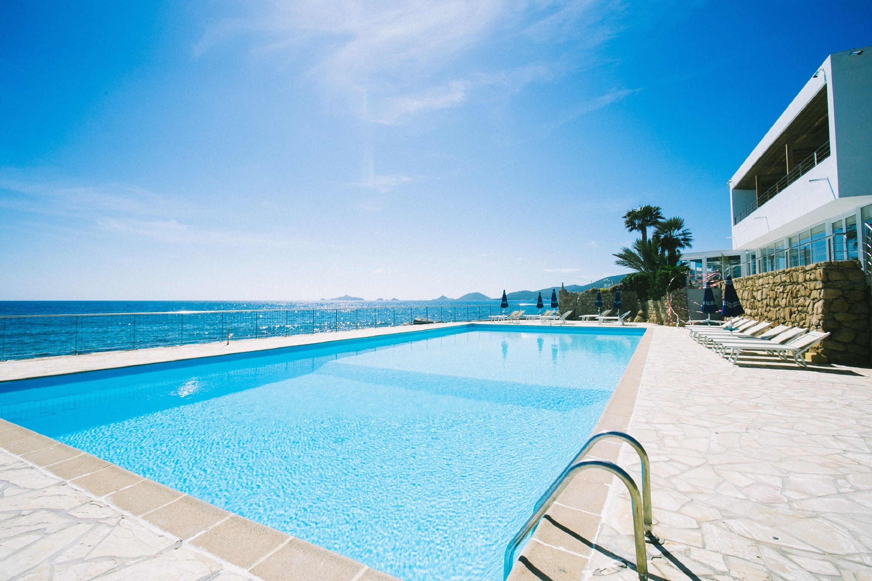 Piscina com vista clara para o oceano e montanhas ao fundo.