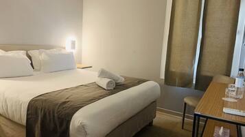 Quarto de hotel com cama, mesa com controle remoto e janela com cortinas.