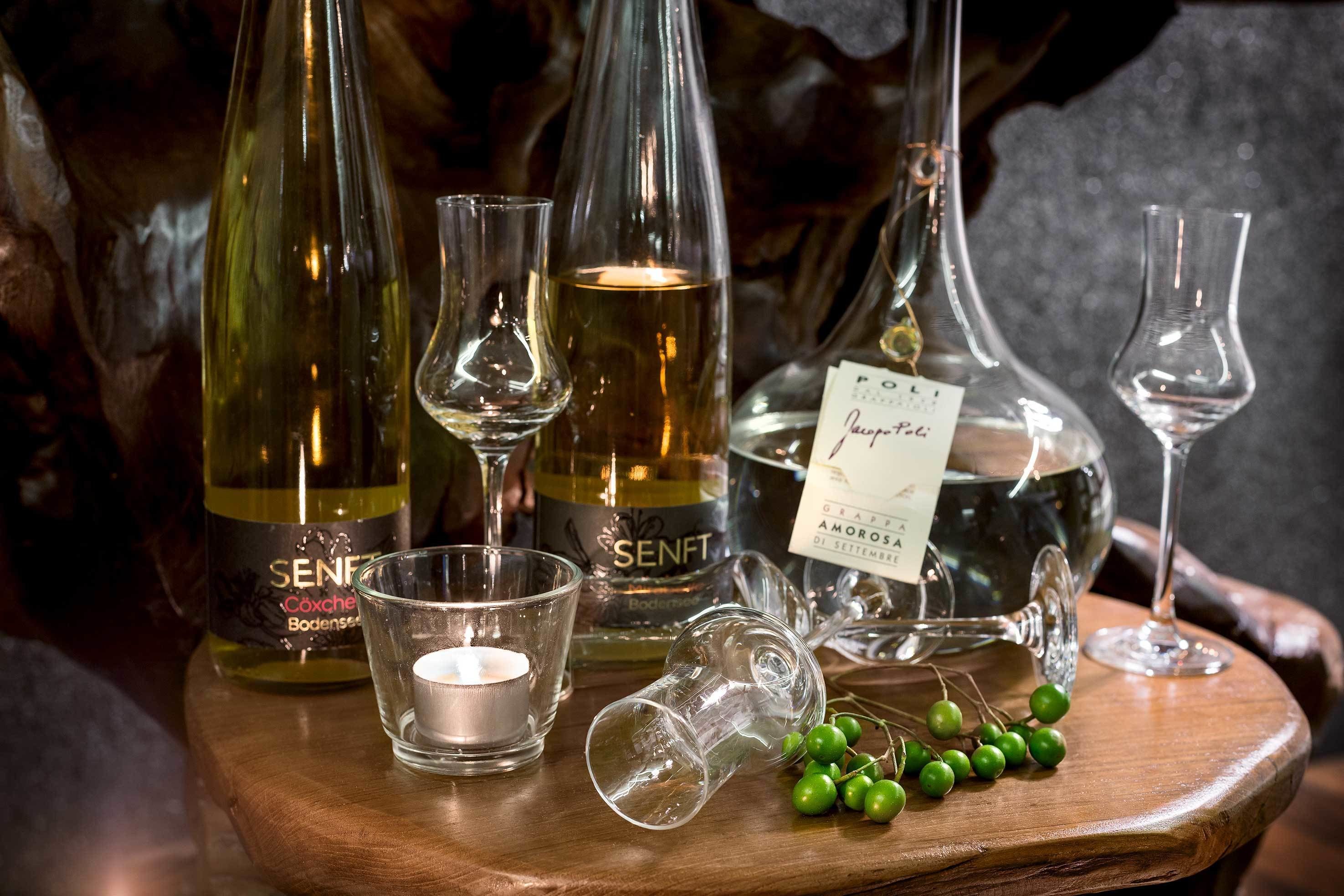 Mesa de madeira com garrafas de vinho, copos e uma vela.