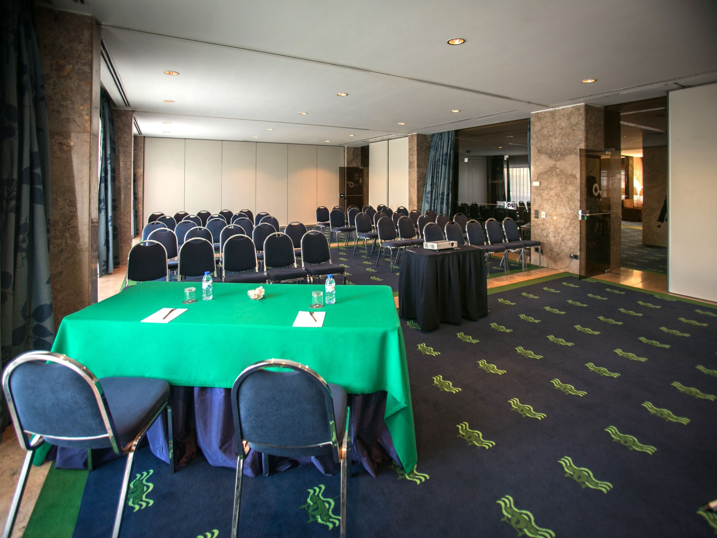 Uma sala de conferências com uma mesa verde, cadeiras e um tapete com padrão verde.