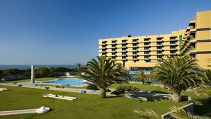 Um hotel com piscina, palmeiras e vista para o oceano.