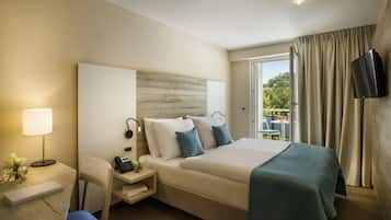 Quarto de hotel com cama, mesa de cabeceira, luminária, cadeira e televisão na parede.