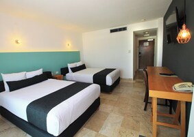 Quarto de hotel com duas camas, uma escrivaninha de madeira, um telefone e um espelho na parede.