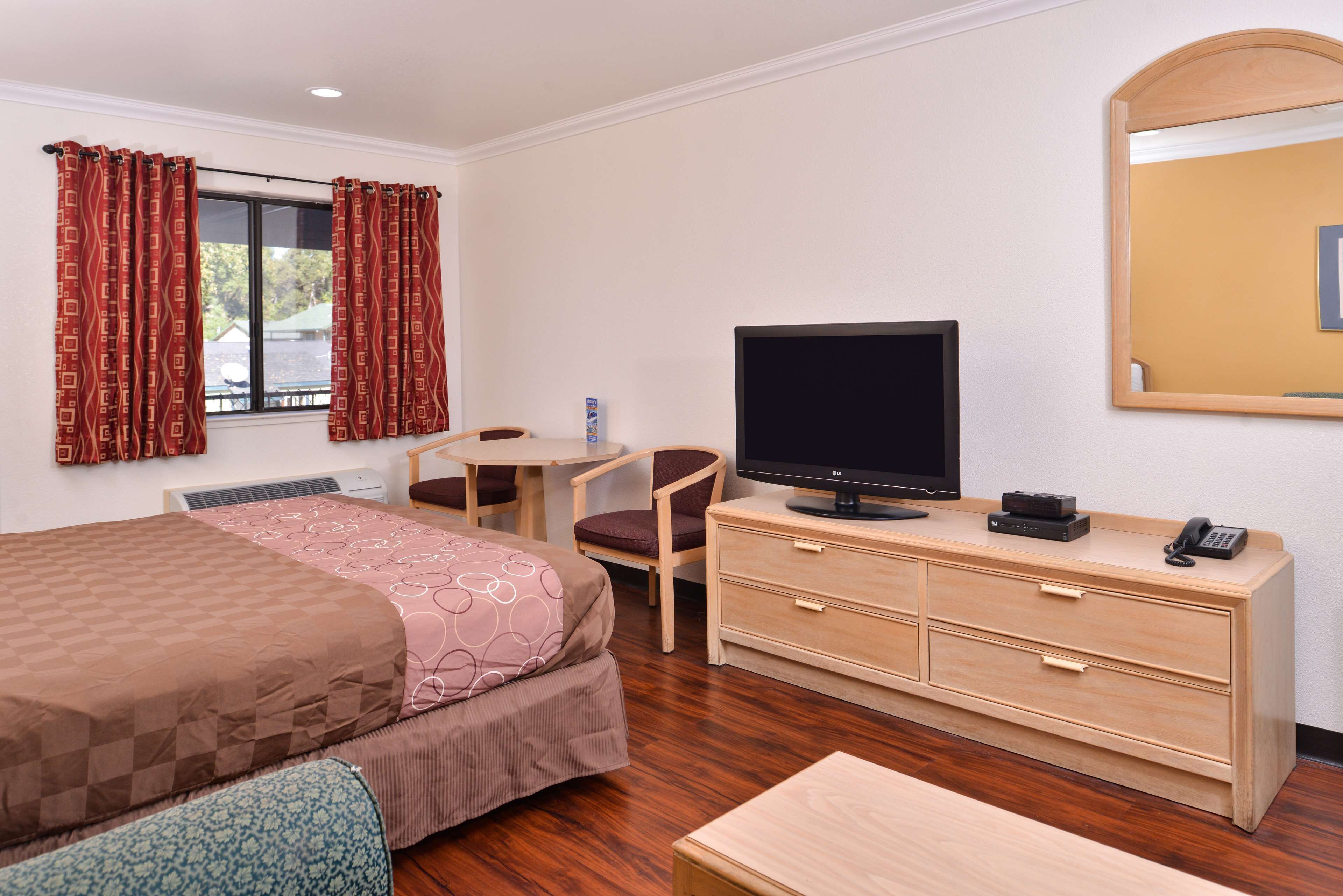 Quarto de hotel com duas camas, uma escrivaninha com cadeira, televisão, cómoda e espelho.