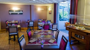 Uma área de refeições com mesas preparadas para dois, cadeiras e um buffet com comida e bebidas.