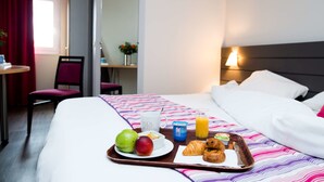 Quarto de hotel com cama, bandeja de café da manhã com frutas, suco, croissants e uma caneca.