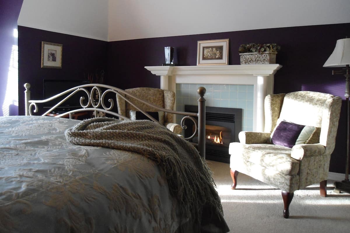 Um quarto com cama, poltrona, lareira e abajur.